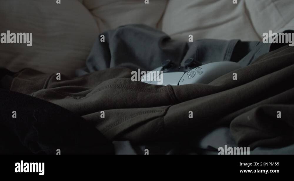 A hand picking up a gaming controller from a pile of clothes. Static ...