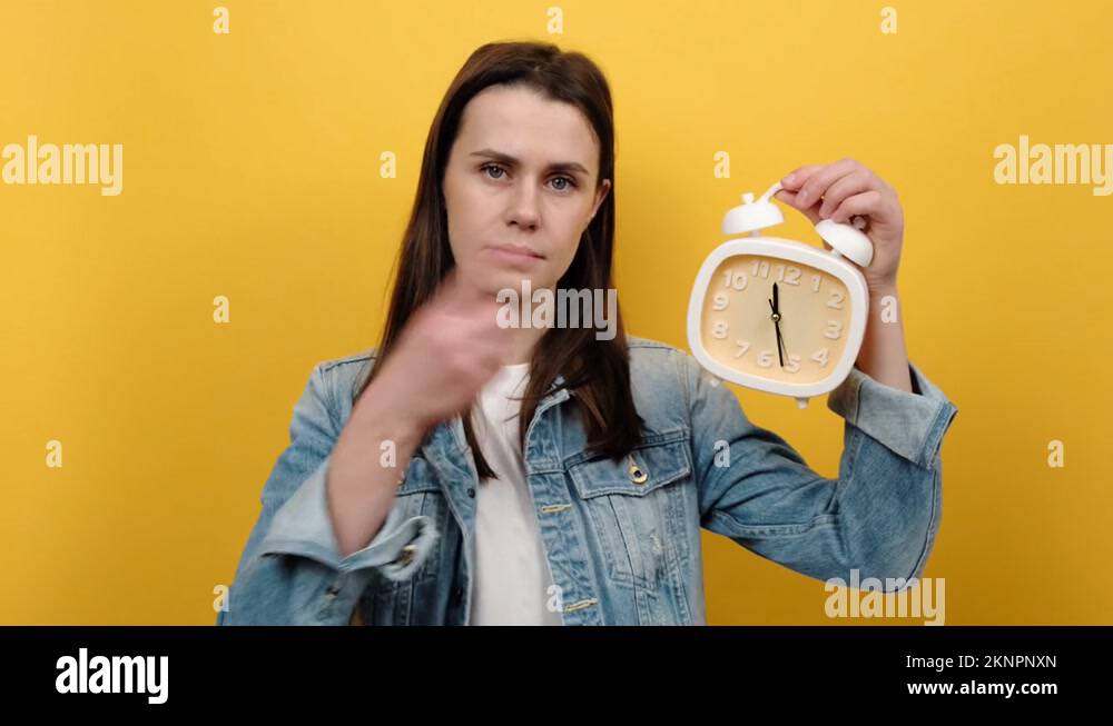 Portrait of strict girl pointing at clock with warning expression, time ...
