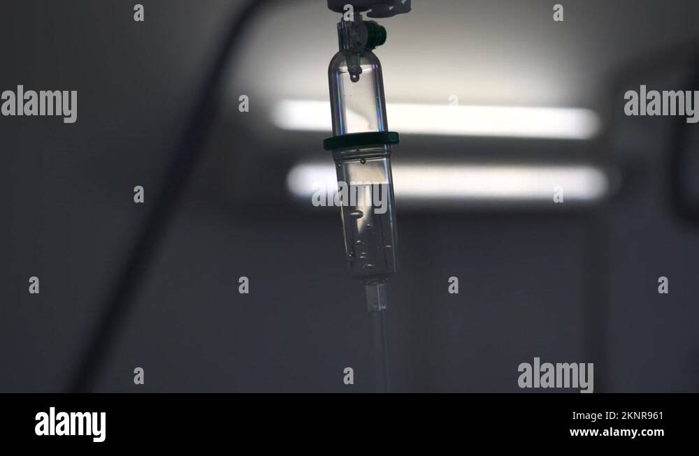 Dolly zoom of an IV drip fluid with white lights int he background ...