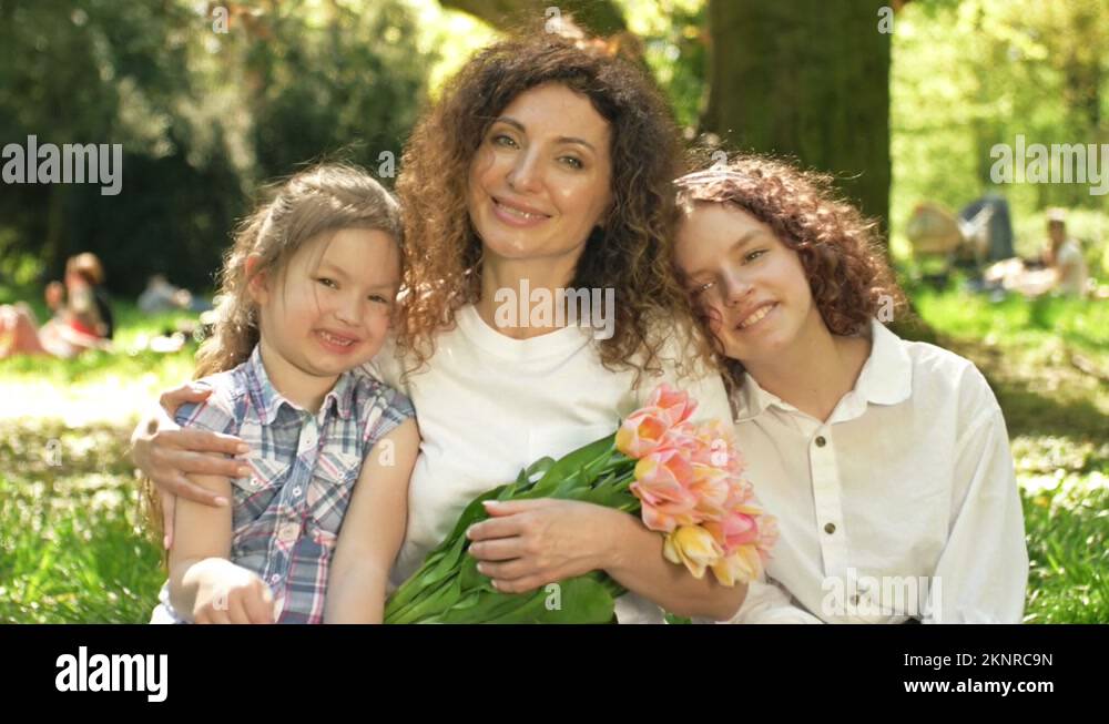 Two girls of different ages hug their mother. The woman is holding a ...
