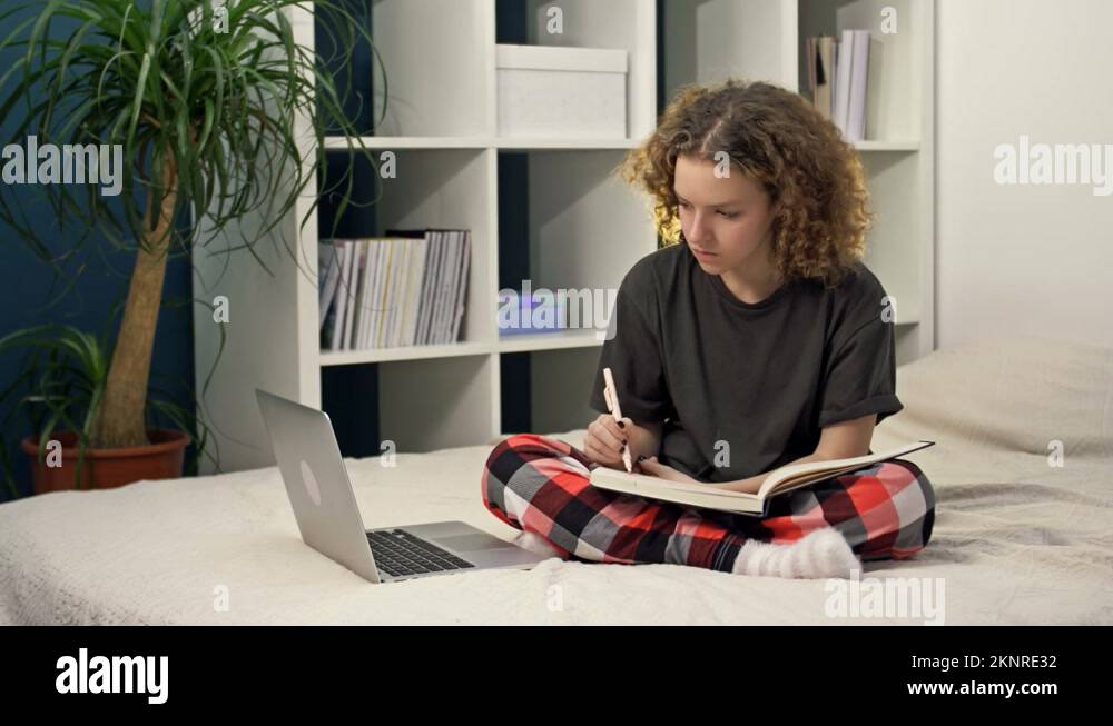 Cute teenage girl doing homework sitting on the bed at home. A young ...