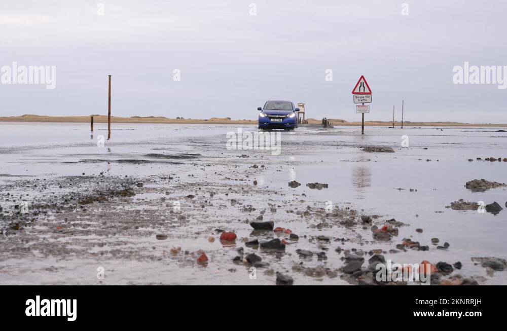 Car driving through salt water along the causeway from holy island ...