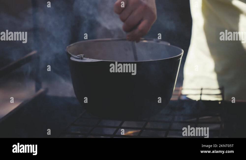 a man cooks food in a pot on fire, delicious cooking in a saucepan in a ...
