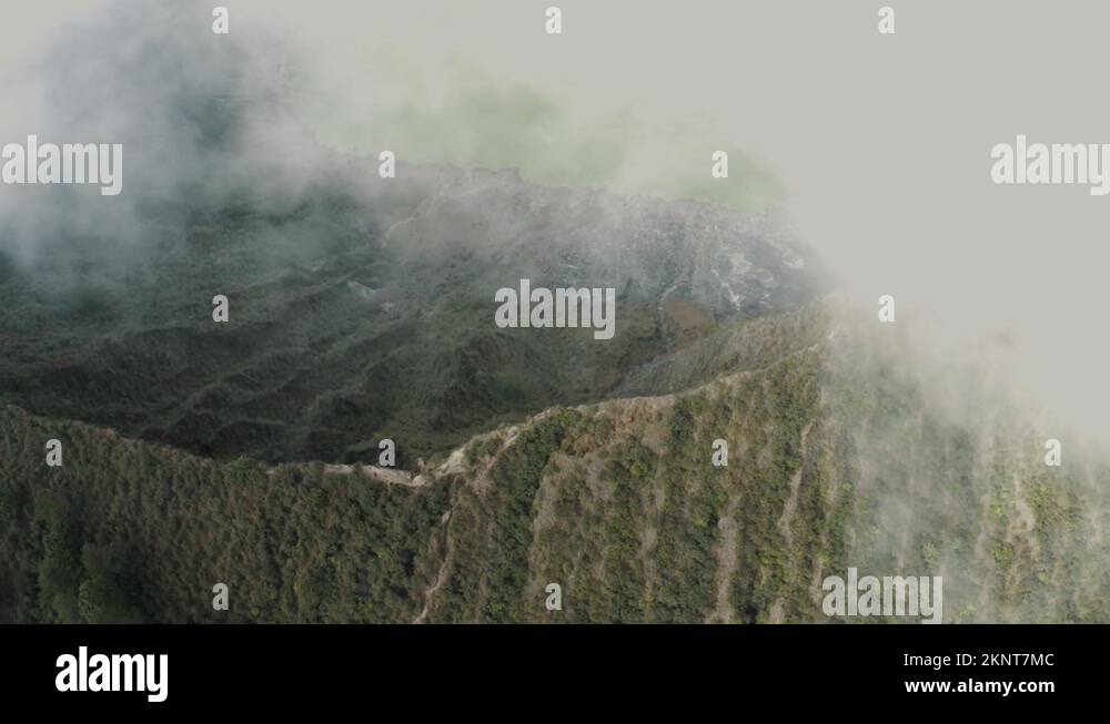 Dense Clouds hiding massive active Volcano with lake in valley during ...