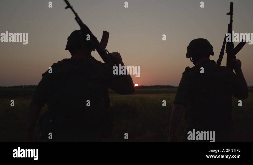 Two military people in special equipment walking across field holding ...