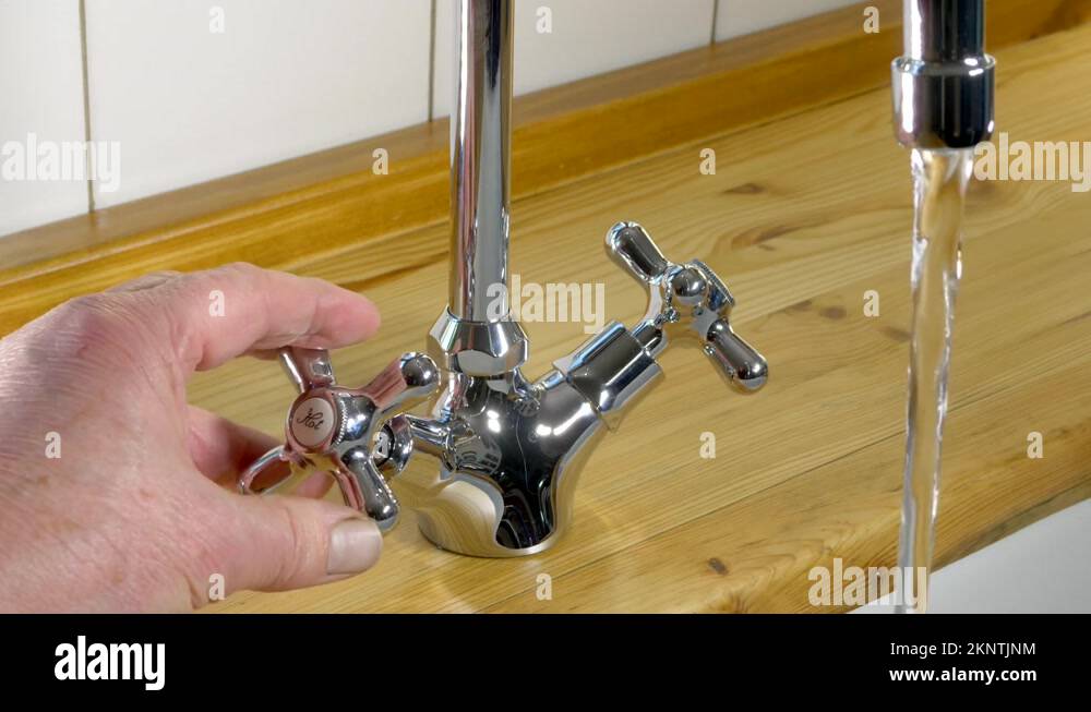 Man's hand turning off a traditional hot tap in a pine kitchen counter ...