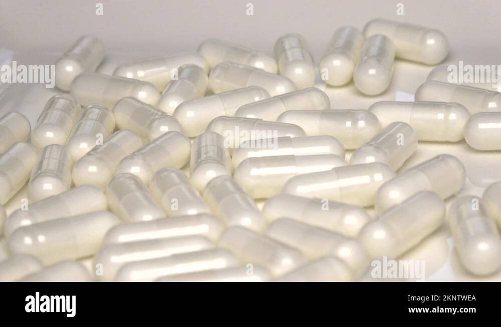 Closeup of many white medical capsules falling down on a plate. 4K ...