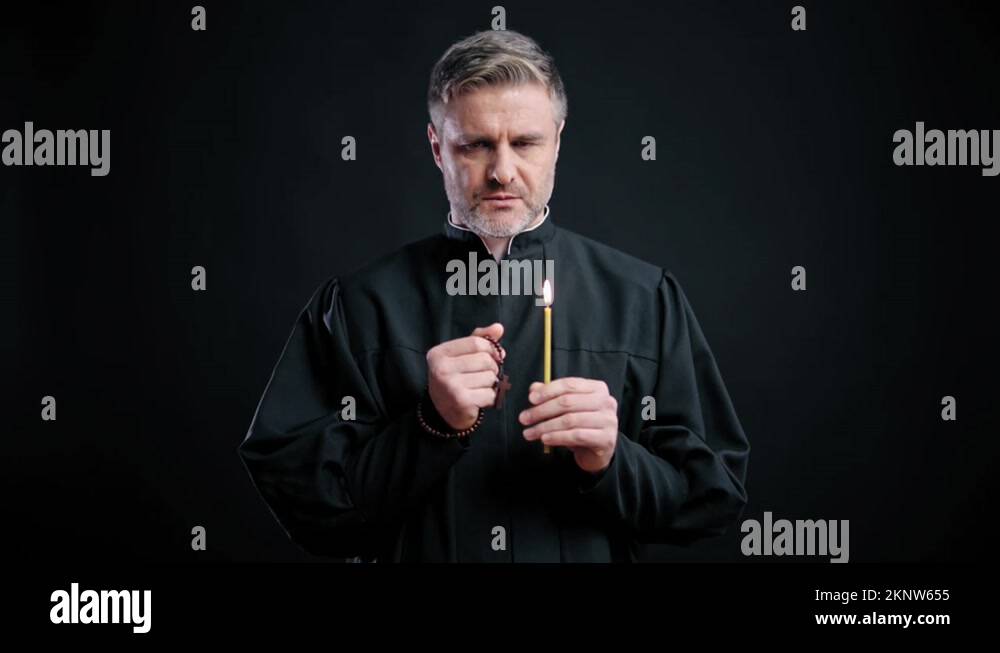 Sad priest praying with rosary and lit candle to commemorate tragedy ...