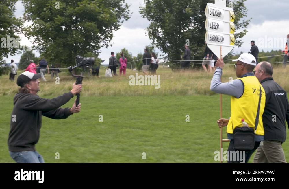 Cameraman recording a man carrying a scoreboard at a golf tournament ...