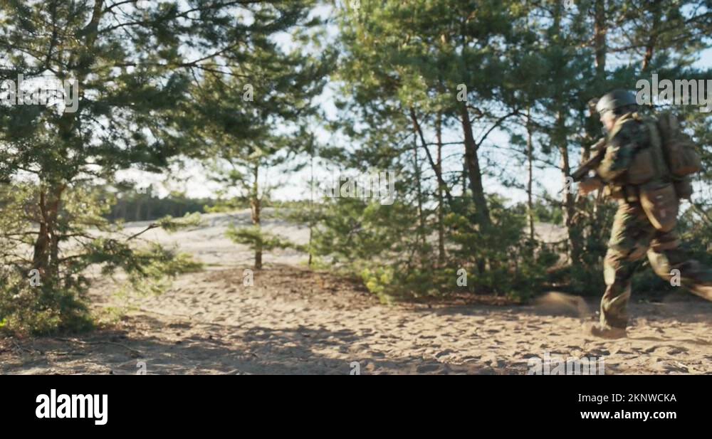 Soldiers run in line on a sandy terrain, on a training ground among ...