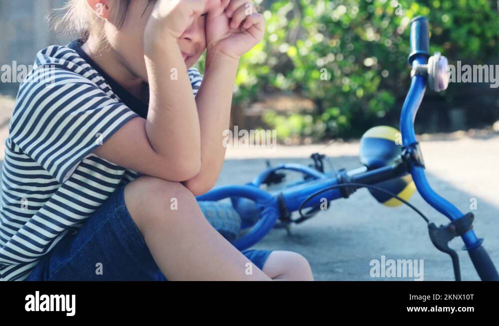 Sad little girl sitting on the ground after falling off her bike at ...