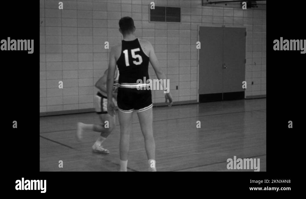 1960s: Gym. Basketball court. Men play basketball backwards. Man holds ...