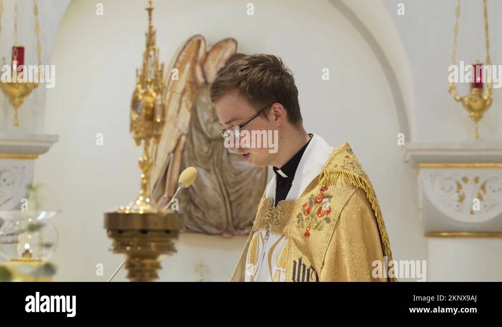 Young priest looks down, reads Bible into microphone at the Holy Mass ...