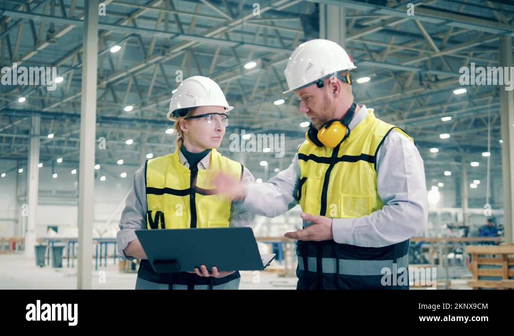 Two factory workers in safety wear are talking to each other. Factory ...
