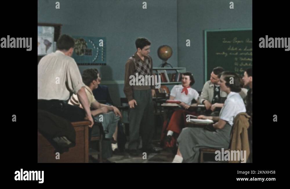 1950s: Man hands instructional model to boy at desk. Hands turn base of ...