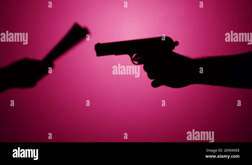 Man holding gun close-up, shadow silhouette of hand with pistol on pink ...