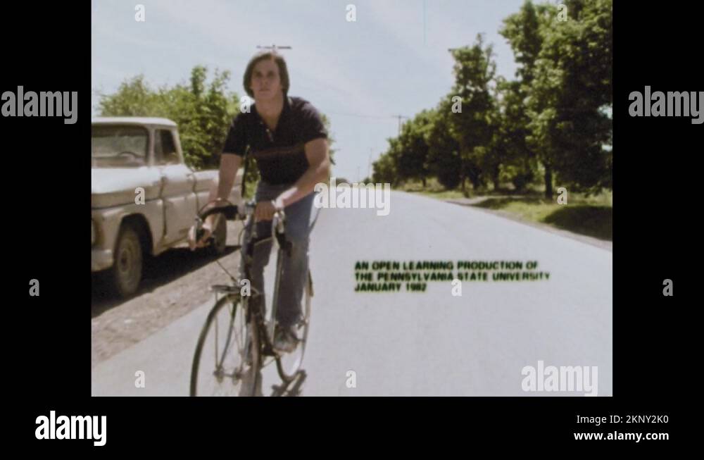1970s: Boy riding his bike, passes cars parked on the road. Car ...