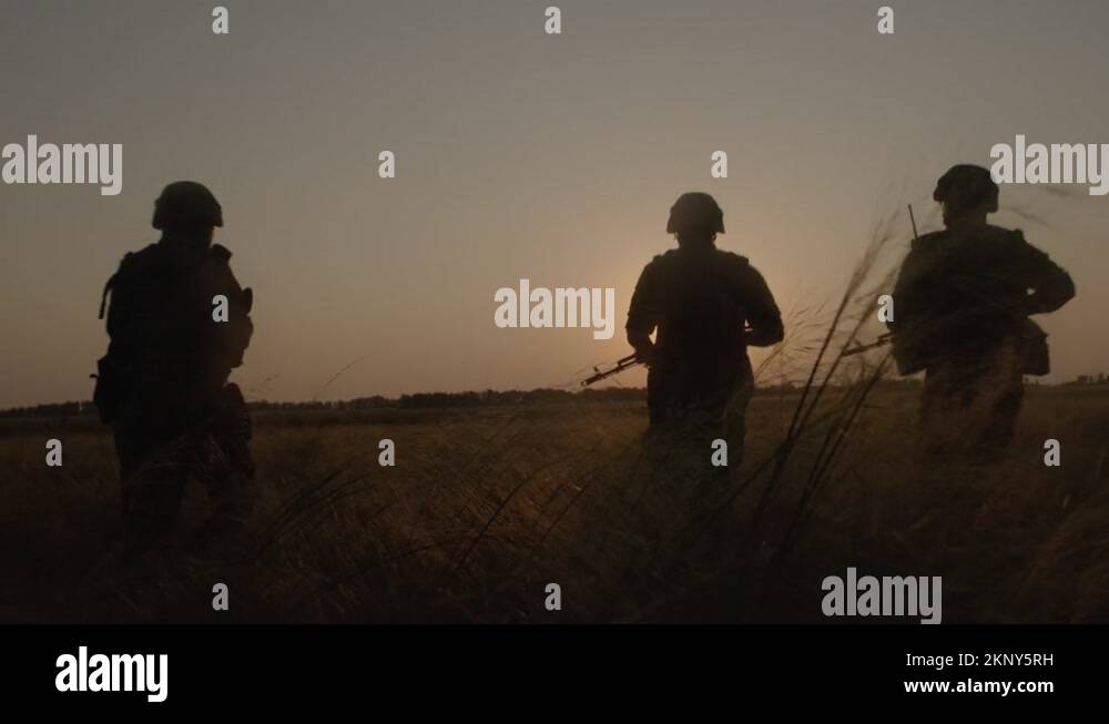 Two armed men with weapon walking across field after combat operation ...