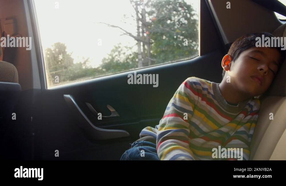 A tired little kid sleeping / resting in the back seat of his car while ...
