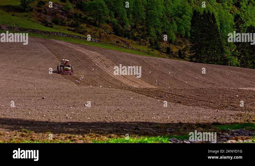 Fast moving shot of tractors ploughing dry and dusty farm field and ...