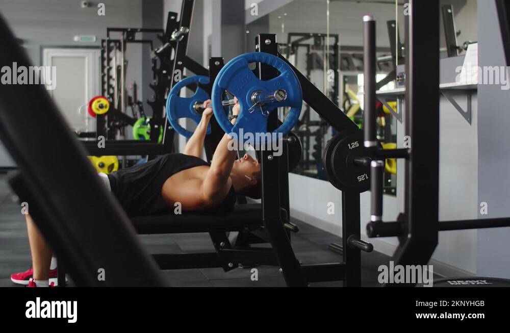 Male bodybuilder trains in gym lying on bench and lifting barbell, side ...