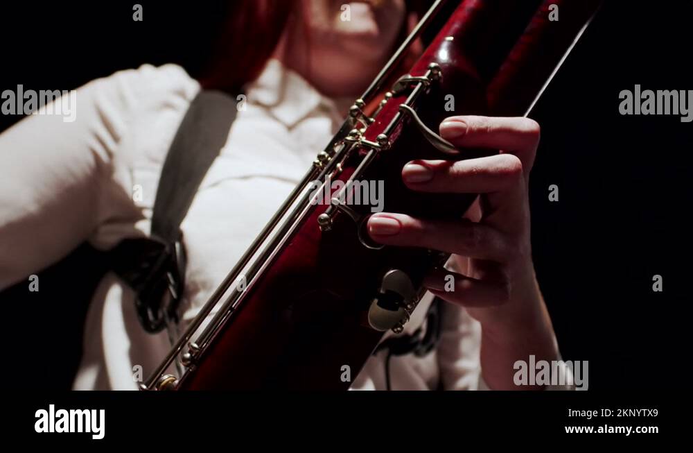 Female musician plays classical music on bassoon while sitting on chair ...