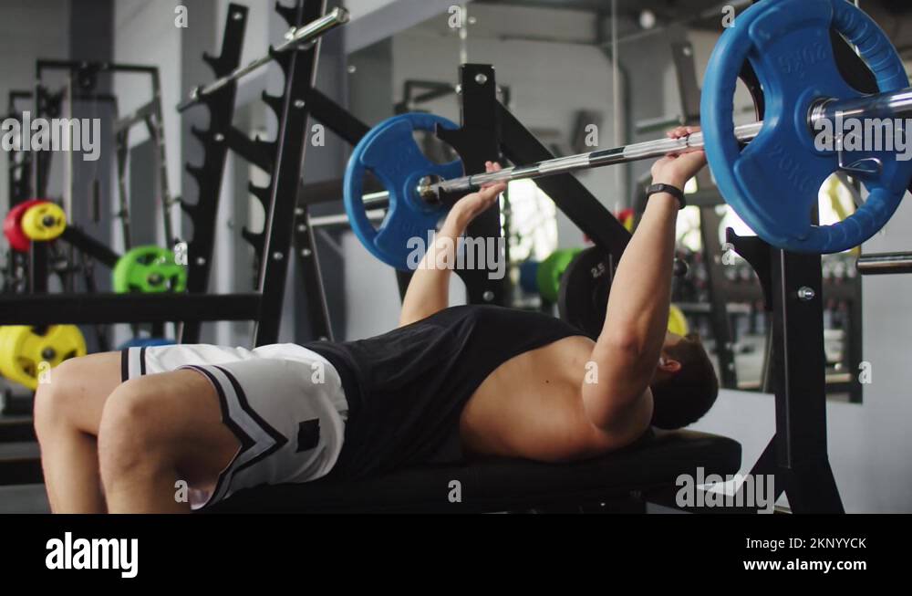 Athletic bodybuilder man trains in gym with barbell lifting it, side ...