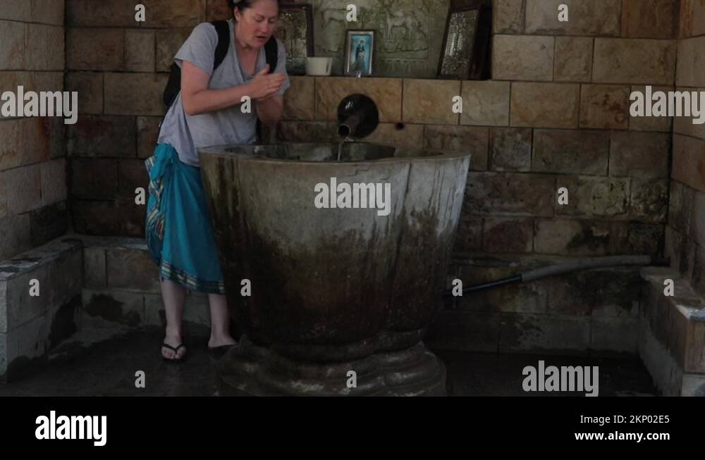 Woman drink water from her hands and wash herself with holy water from ...