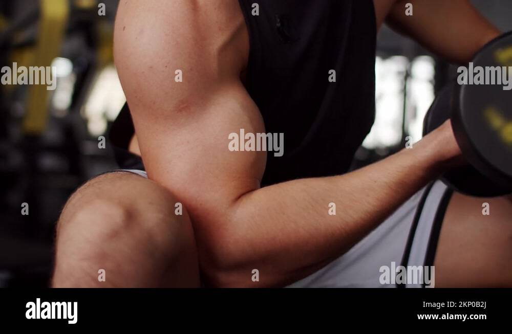 Closeup of muscular mans arm training biceps in gym lifting dumbbell ...