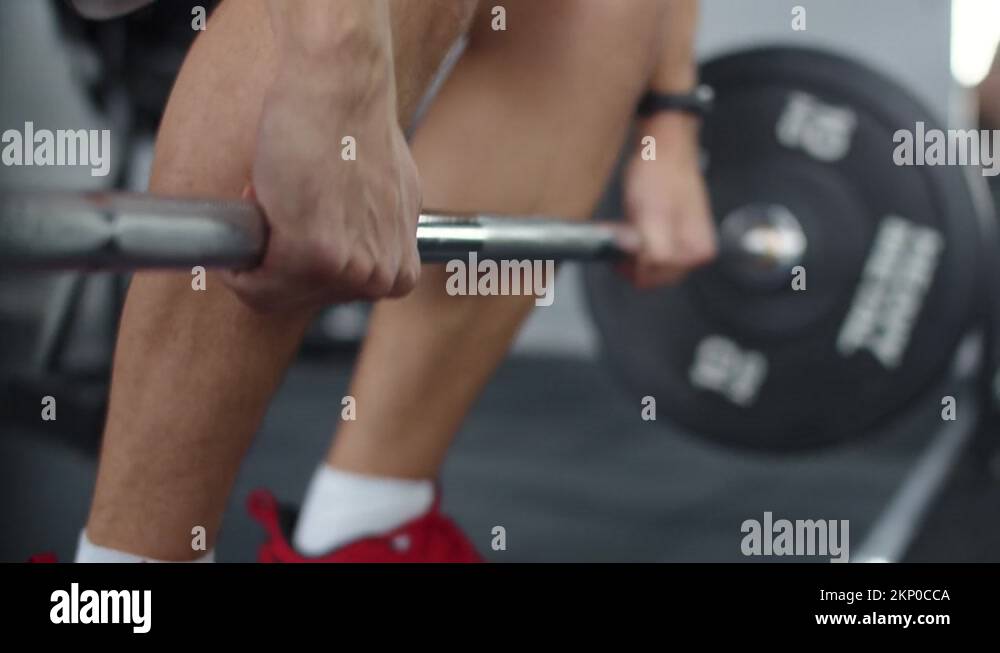 Closeup of hands of athletic man grabbing and lifting barbell at gym ...