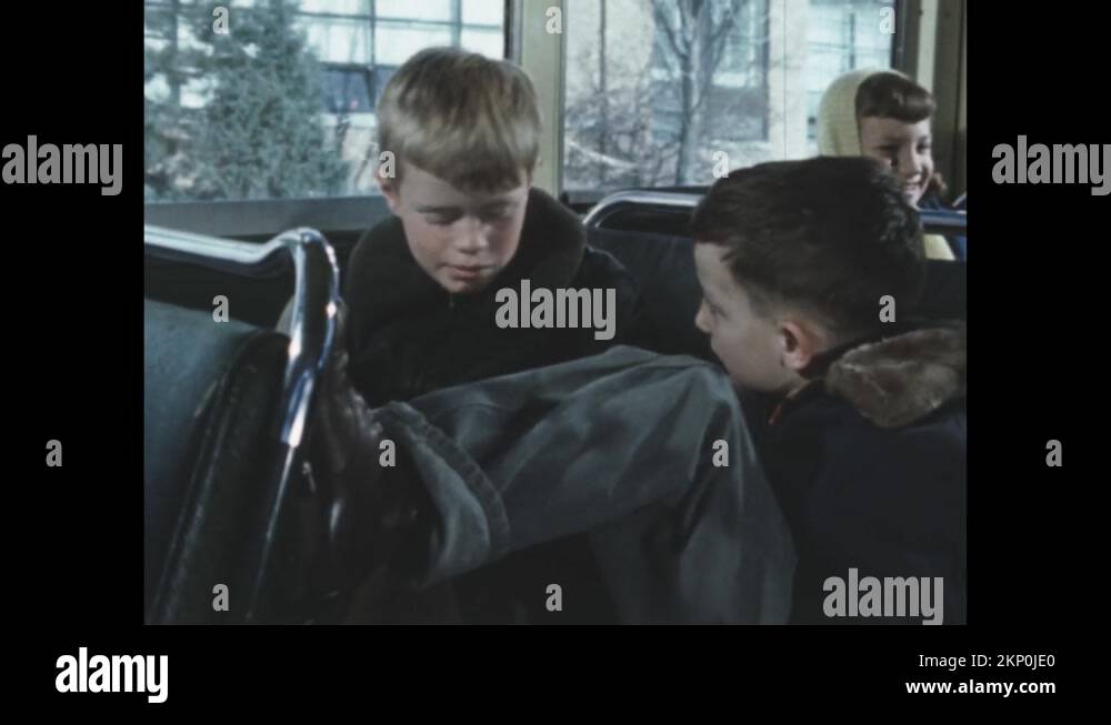 1950s: Little boys sit down on bus. Boy puts foot on bus seat. Hand ...