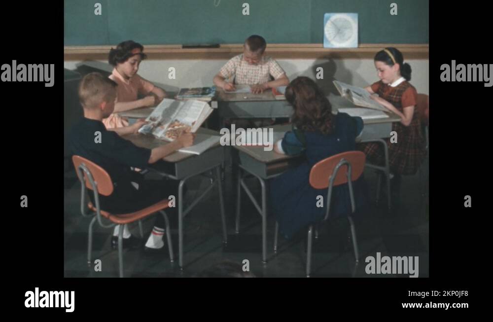 1960s: Classroom. Group of students sit at desks and work. Hand holds ...
