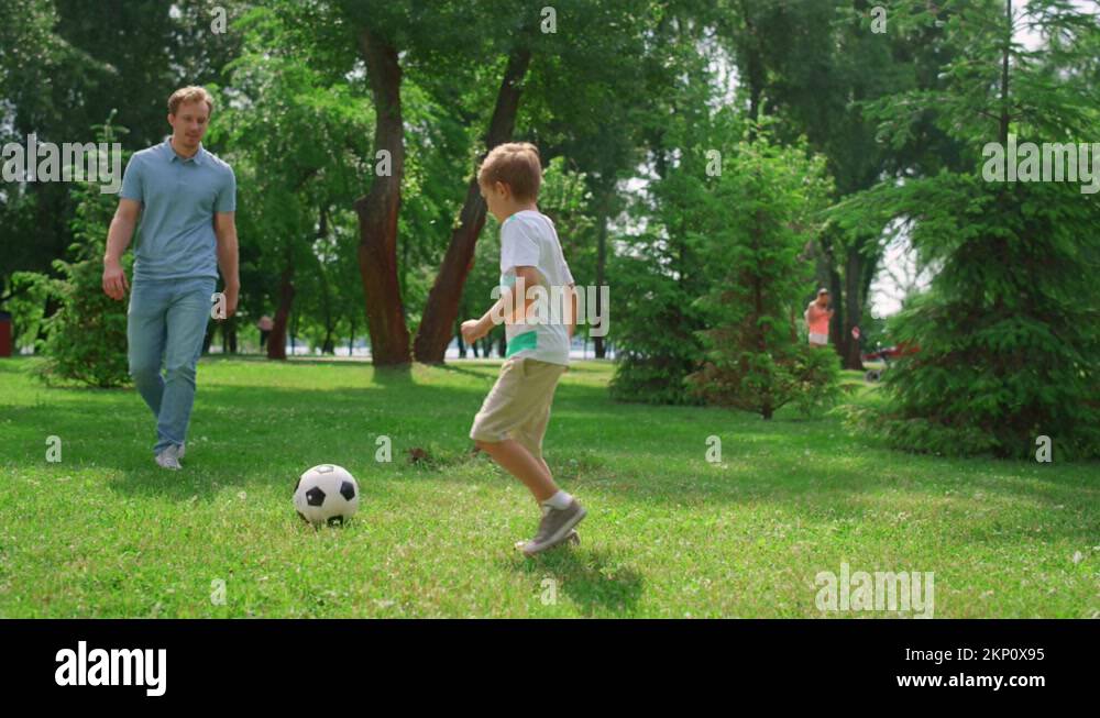 Sporty man passing ball to active son on green park. Father play soccer ...