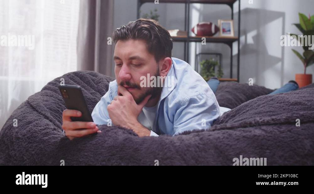Close up portrait of adult man lying on his stomach on sofa scrolling social Stock Video Footage ...