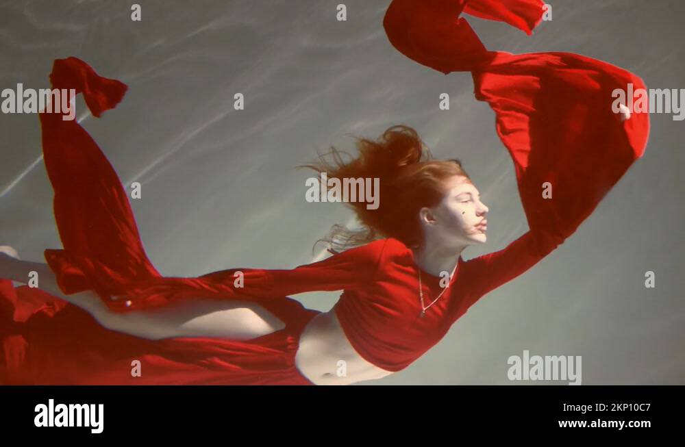 Attractive red-haired young woman swims beautifully underwater in a red ...