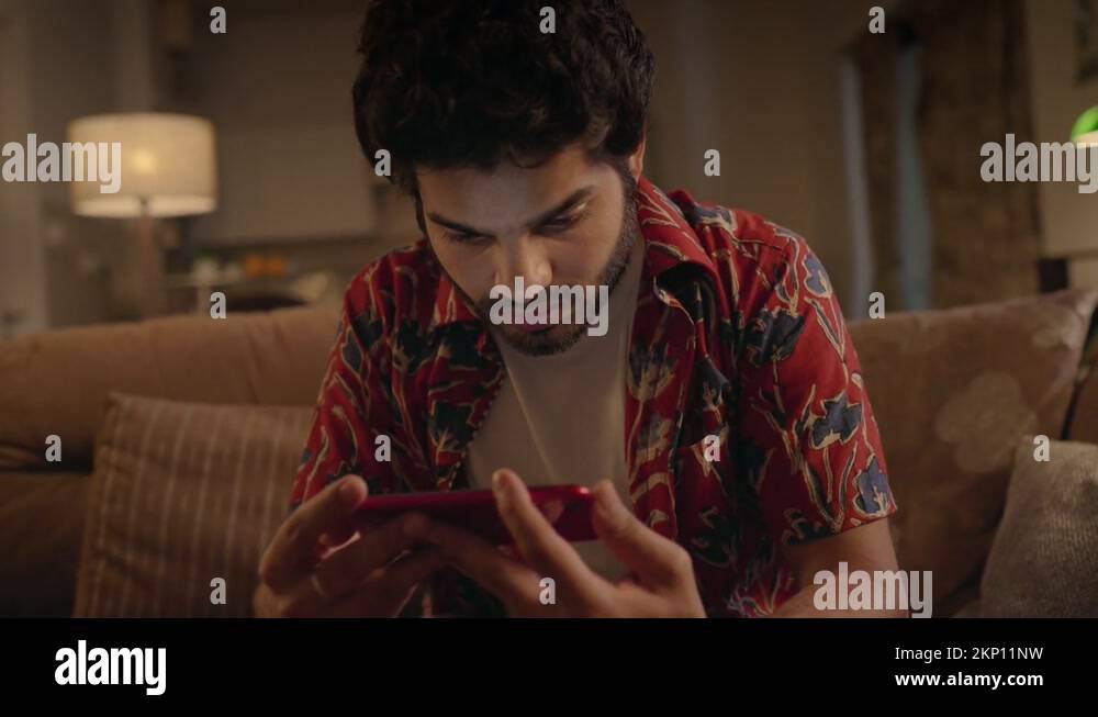 Indian Man sitting on couch watching live cricket match on Mobile phone ...