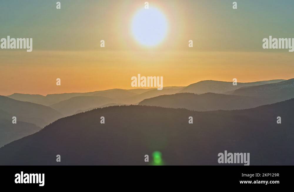 Sun moves across golden sky, sets behind mountains; high elevation time ...