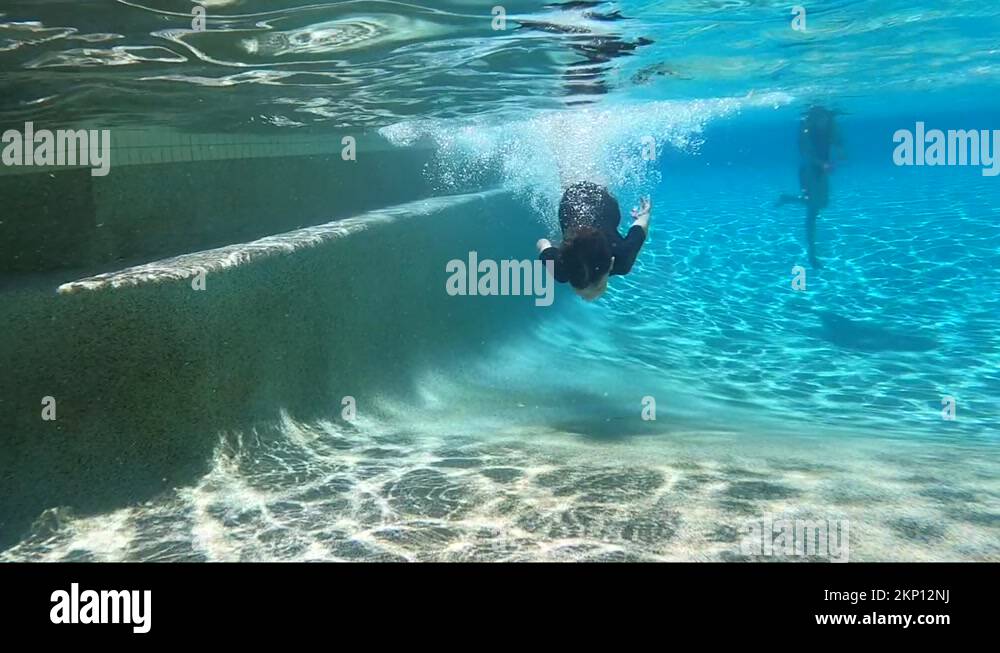 A young boy dives to the bottom of a deep public pool, swimming ...