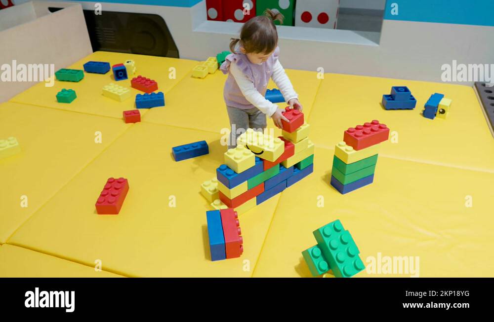 Adorable little girl stacking big constructor bricks building a wall on ...