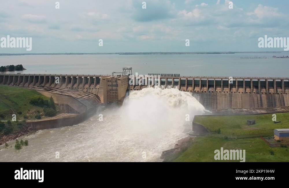 Revealing shot of lake behind reservoir wall with open sluice gates ...