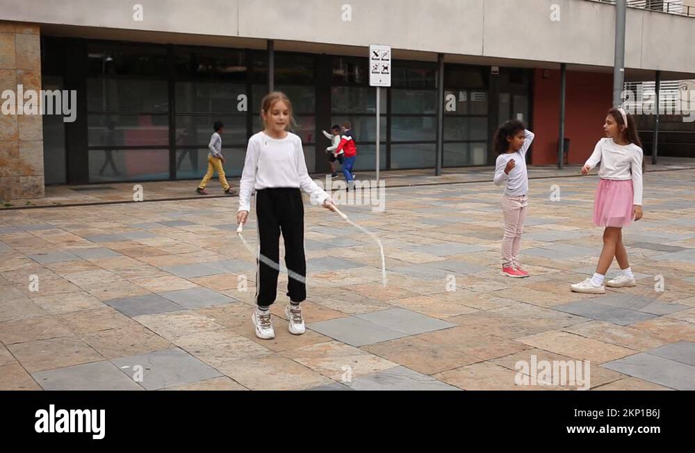 Cheerful sporty tween girl jumping rope in school yard during recess in ...