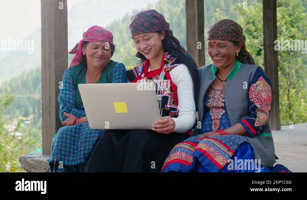 Three cheerful rural Indian women in traditional attire sitting using a ...