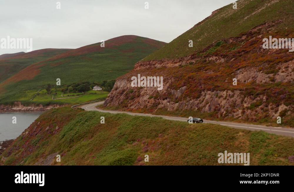 Car driving on coastal road around rock wall on one side and steep ...