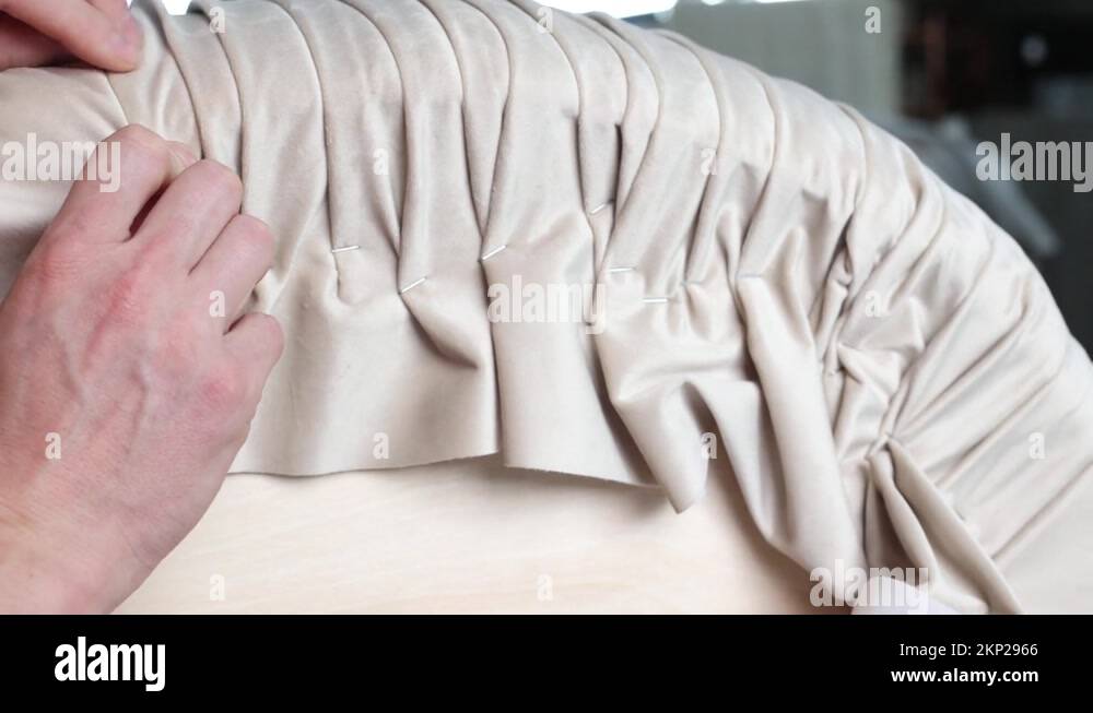 Process of pleating or draping beige fabric by hand on a furniture pouf ...