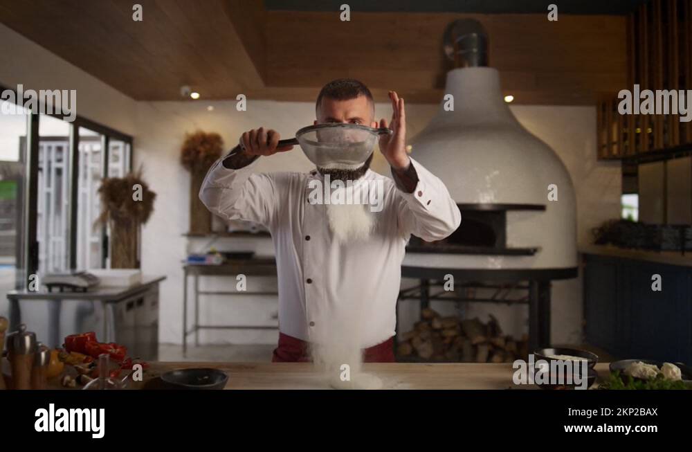 Handsome chef sifting flour using sieve in kitchen. Man cooking in ...
