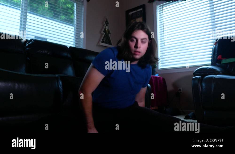 Man sits at home and stretches with his legs out wide in a straddle ...