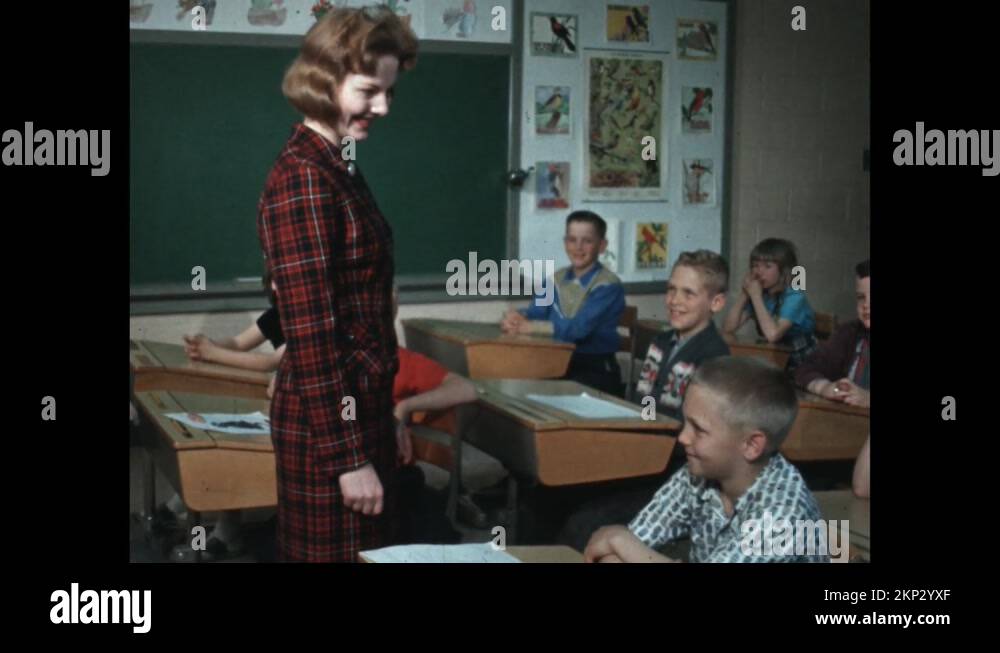 1960s: Teacher stands in classroom of kids, smiles and speaks. Little ...