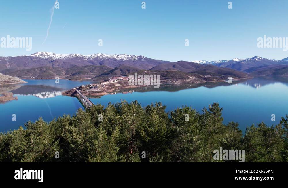 Long bridge over huge, crystal clear blue lake. Lower third of forest ...