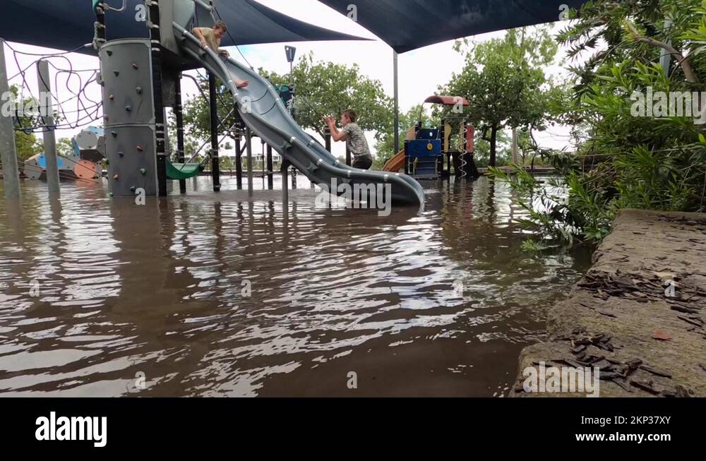 Two happy young boys splashing and playing in a flooded playground ...