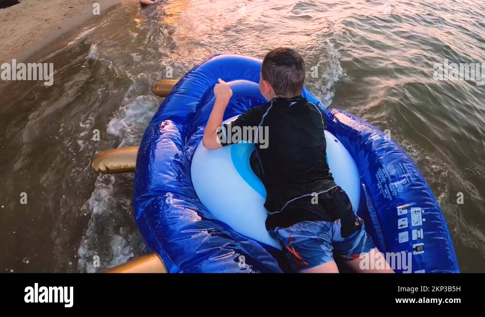 A smiling little boy is dragged through the water, laying on an ...